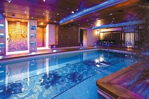 Piscina interior moderna com deck de madeira e parede de vidro.