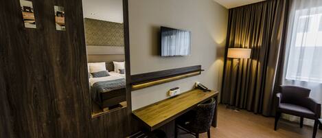 Quarto de hotel com cama, escrivaninha, cadeira, luminária e um espelho grande.