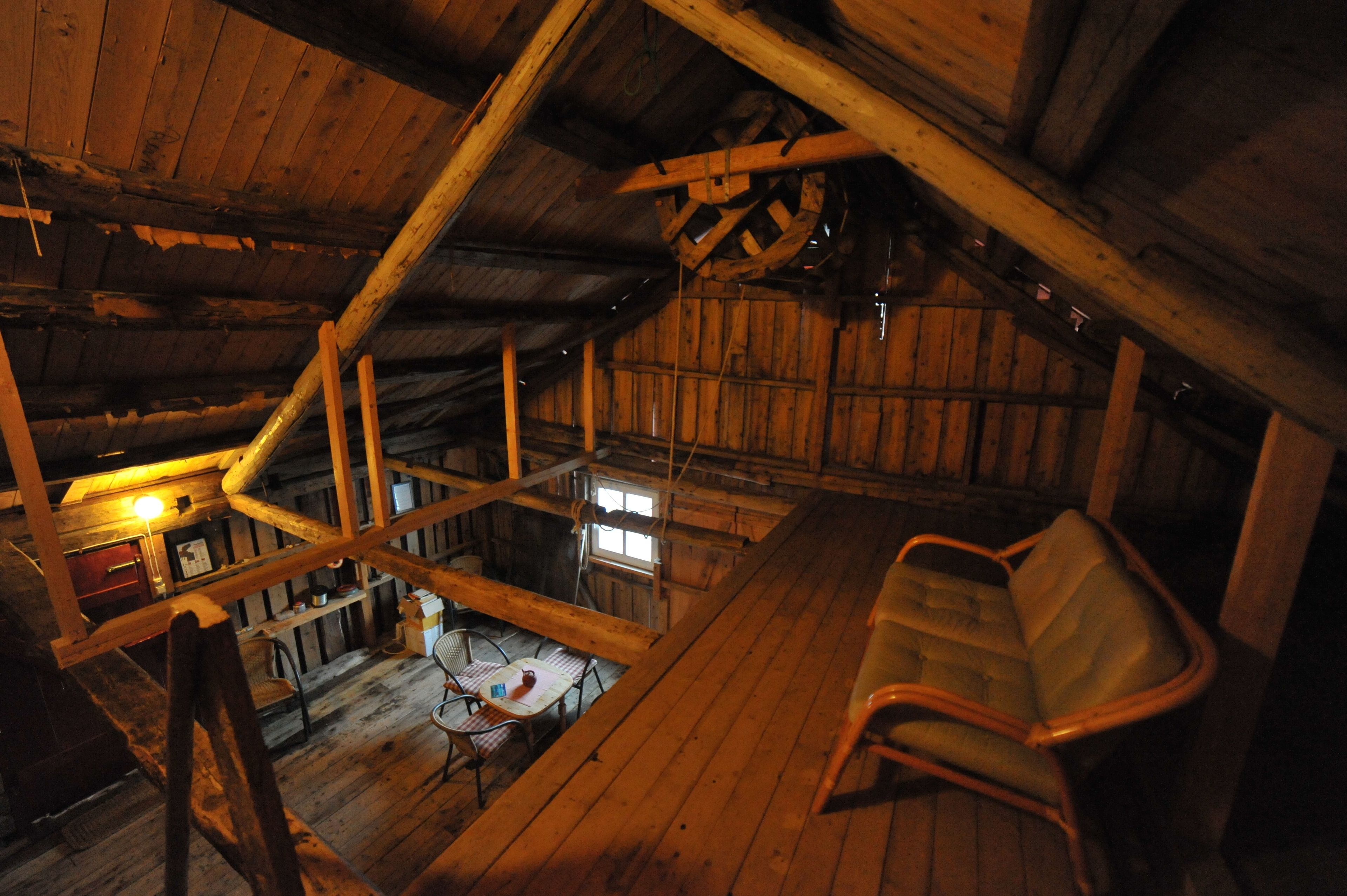 Interior rústico de uma cabana de madeira, com mezanino, mesa de jantar e uma cadeira acolchoada.