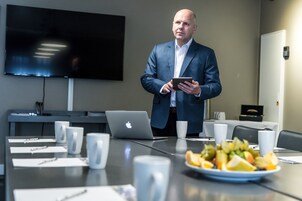 Uma sala de conferências com um homem segurando um tablet, um laptop e um prato de frutas na mesa.