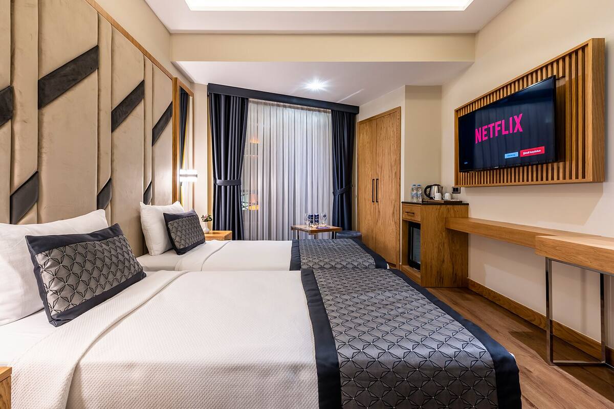 Quarto de hotel com duas camas, uma televisão, secretária de madeira e minibar.