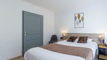 Quarto de hotel bem arrumado com cama, uma cadeira, mesa de cabeceira com abajur e porta.