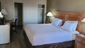 Quarto de hotel com uma cama grande, uma mesa de trabalho com abajur, uma cadeira, um guarda-roupa e uma mesa de cabeceira com abajur.
