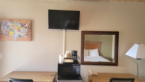 Quarto de hotel com teto de madeira, televisão na parede, obra de arte com um mapa, cama com cabeceira de madeira, mesa de cabeceira com abajur e escrivaninha com cadeira.