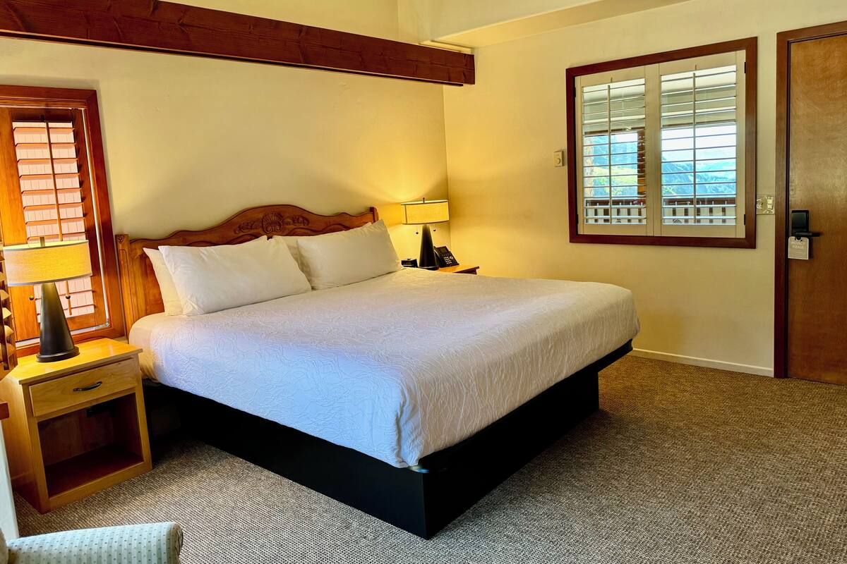 Quarto de hotel com uma cama grande, cabeceira de madeira, duas luminárias de cabeceira, mesa de cabeceira, placa de aviso de privacidade e uma janela com persianas.