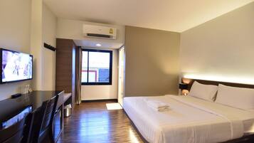 Quarto de hotel com cama, escrivaninha, televisão e ar condicionado.