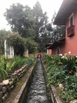 Um canal de água estreito ladeado por vegetação exuberante e um edifício vermelho com varanda.