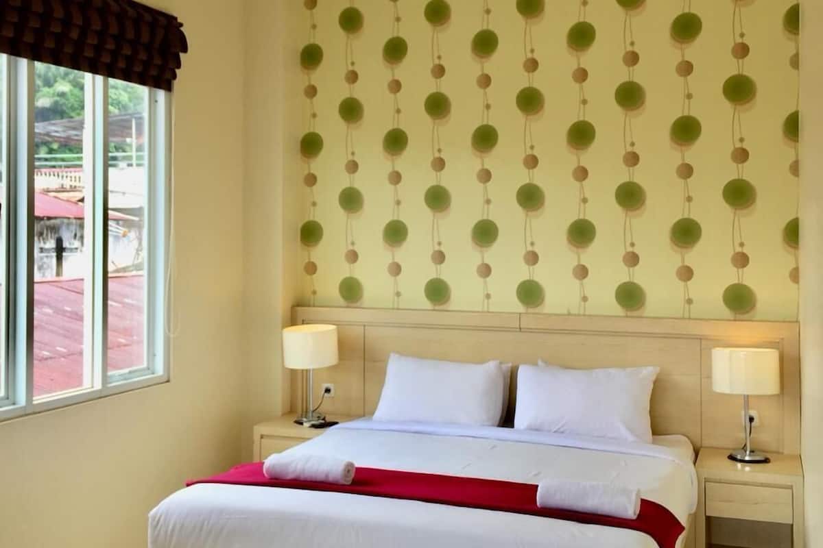 Quarto de hotel com cama, duas mesas de cabeceira, janela com vista e parede estampada.