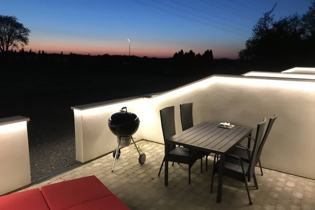 Um pátio externo com mesa e cadeiras, um sofá vermelho e uma churrasqueira.