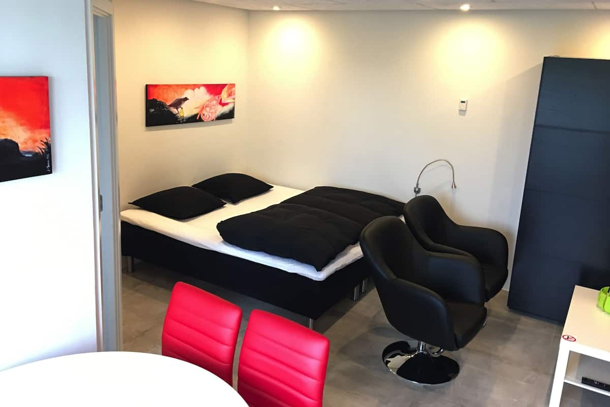 Um quarto moderno com uma cama, duas cadeiras vermelhas, uma cadeira preta, uma escrivaninha e um quadro na parede.