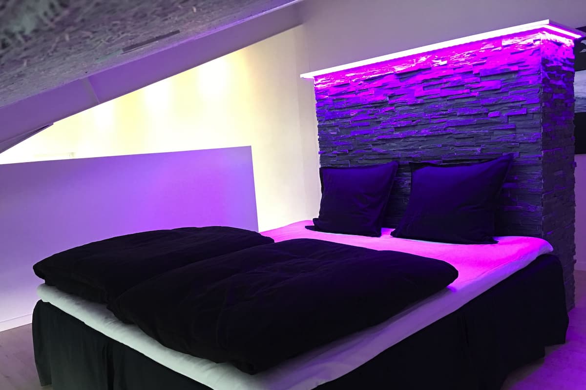 Quarto com cabeceira de pedra, duas camas pretas com roupa de cama branca e teto inclinado.