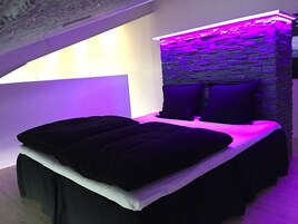Quarto com cabeceira de pedra, duas camas pretas com roupa de cama branca e teto inclinado.