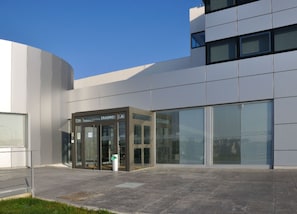Um edifício moderno com entrada de vidro, céu claro e área pavimentada na frente.