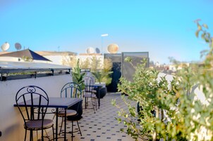 Um pátio no terraço com área de estar ao ar livre, incluindo cadeiras e mesas de metal, rodeado por vasos de plantas e piso estampado.