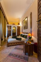 Quarto tradicional com uma cama grande, uma mesinha de madeira com frutas e um tapete estampado.