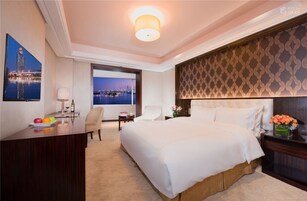 Quarto de hotel com uma cama grande, uma escrivaninha com cadeira, uma televisão e vista para a cidade.
