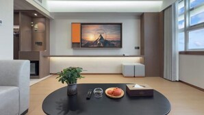 Uma sala de estar moderna com uma mesa de centro preta, uma planta, um controle remoto e uma cesta de frutas.