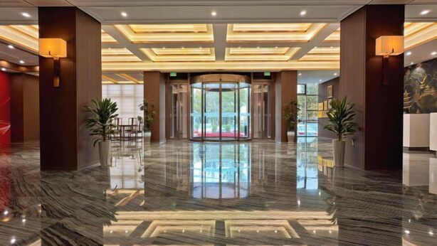 Um hall de hotel com piso de mármore, porta giratória e plantas em vasos.