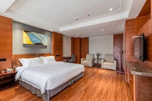 Quarto de hotel com uma cama grande, televisão, escrivaninha e área de estar.