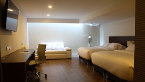 Quarto de hotel com escrivaninha, duas camas, uma cadeira e televisão.