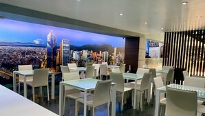 Um restaurante moderno com vista panorâmica da cidade, mesas e cadeiras brancas e um design de interiores elegante.