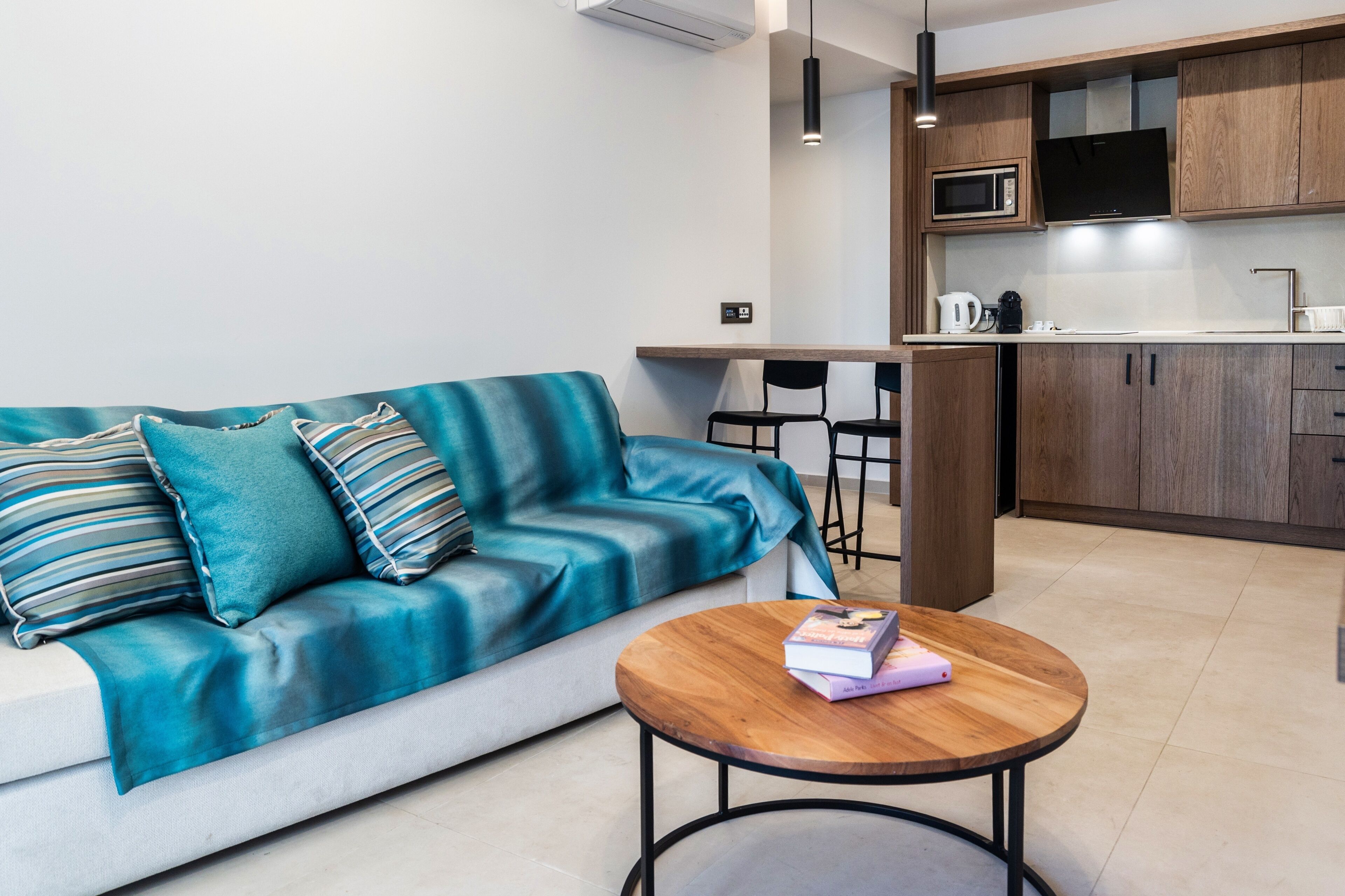 Uma sala de estar moderna com um sofá, uma mesa de centro e uma cozinha com armários de madeira e micro-ondas.