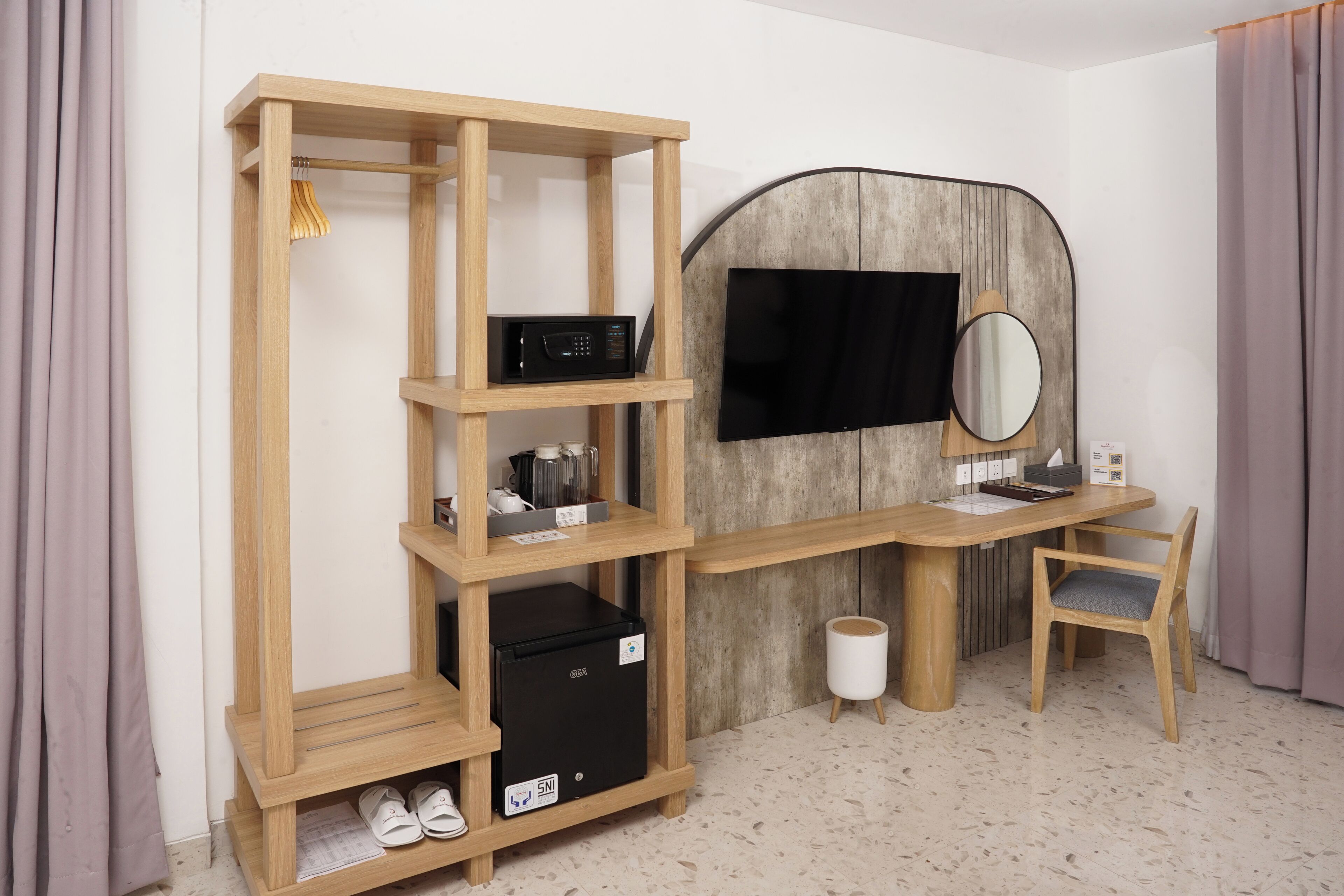 Quarto de hotel compacto com escrivaninha de madeira, televisão, espelho, armário pequeno e sapateira.