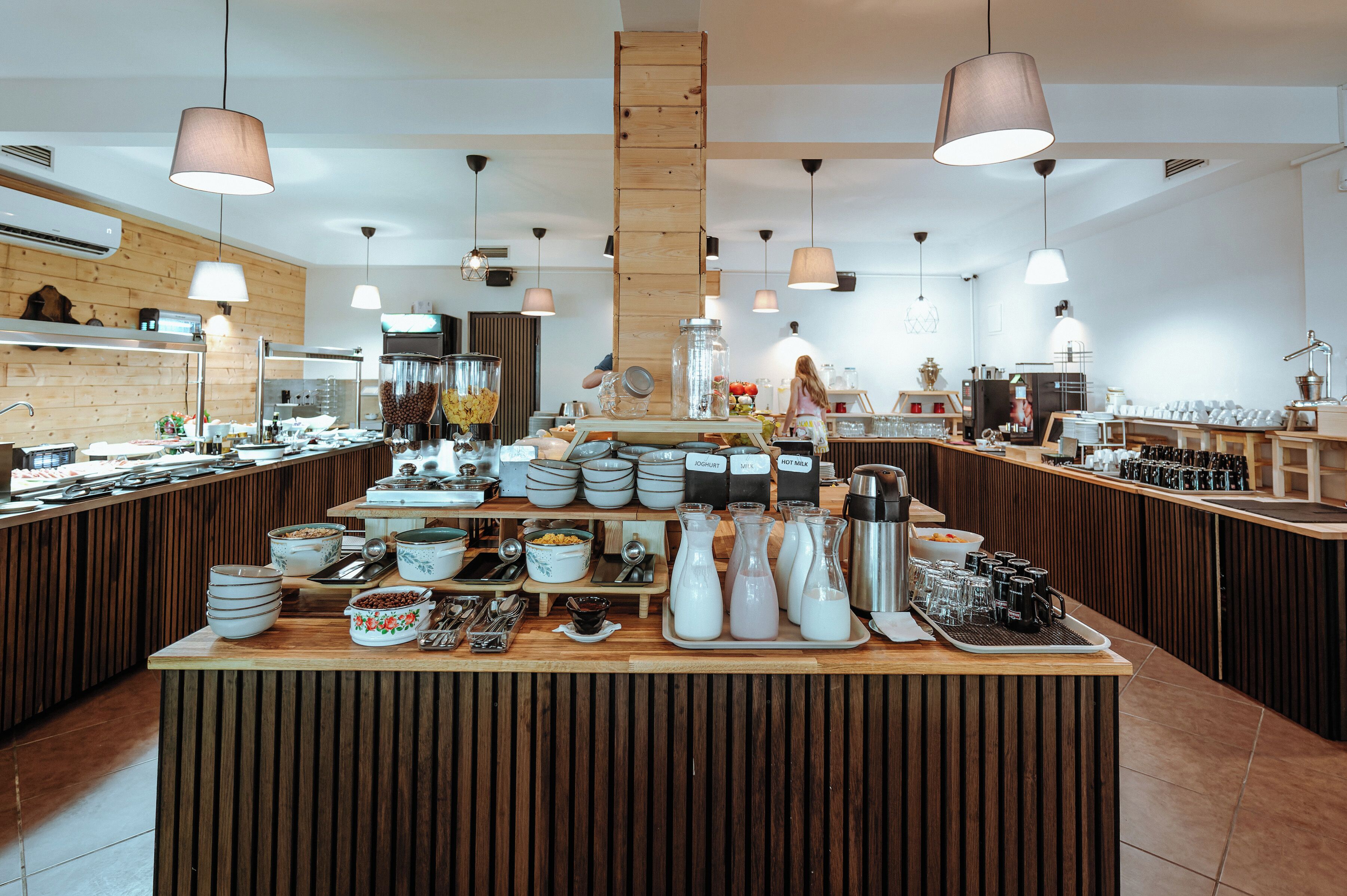 Um buffet de café da manhã moderno, com diversos alimentos e bebidas, detalhes em madeira e iluminação pendente.