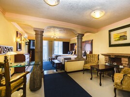 Quarto de hotel com uma cama grande, duas mesas de cabeceira, uma escrivaninha com uma cadeira, uma lareira e um vaso grande.