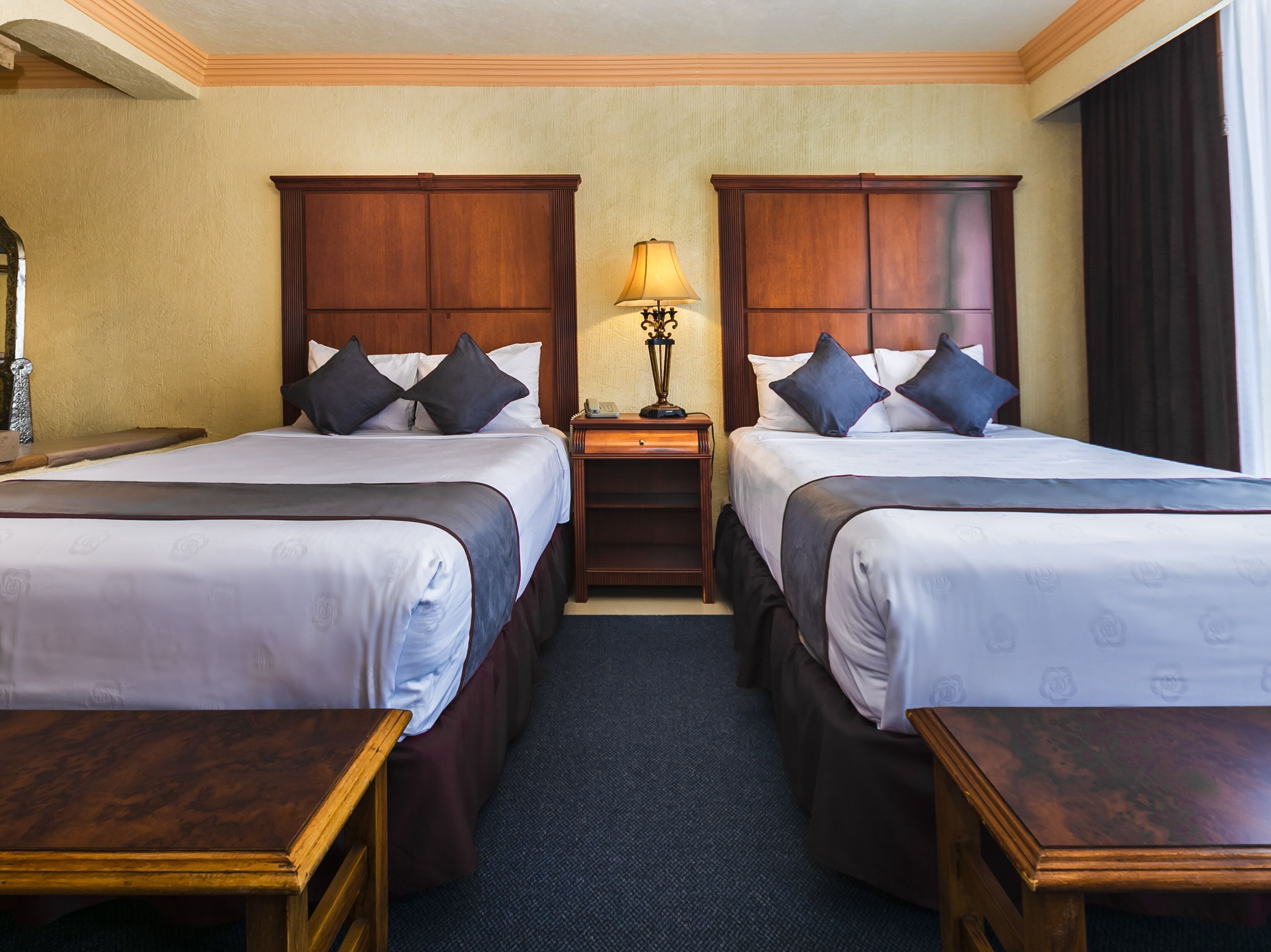 Quarto de hotel com duas camas, uma mesa de cabeceira com abajur e cabeceira de madeira.