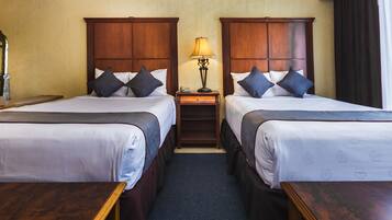 Quarto de hotel com duas camas, uma mesa de cabeceira com abajur e cabeceira de madeira.