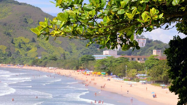Uma praia com pessoas, guarda-sóis e edifícios ao fundo.