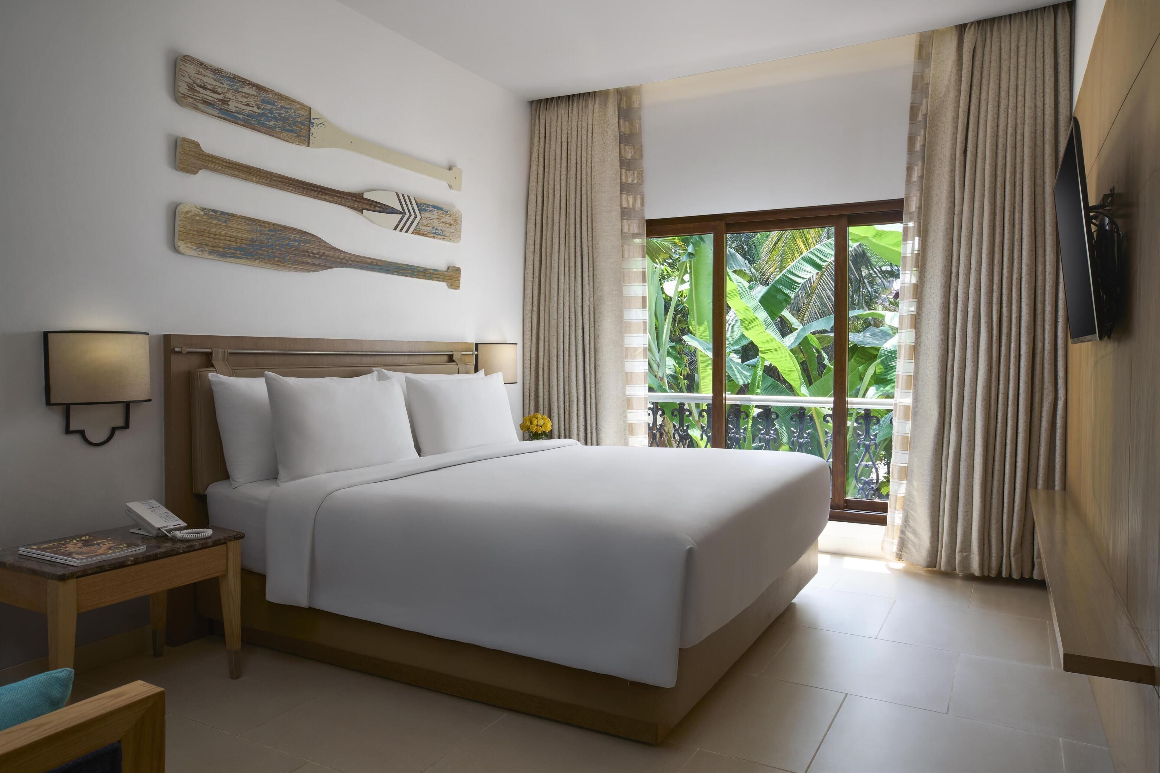 Quarto de hotel com cama, mesa de cabeceira, televisão e janela com cortinas.