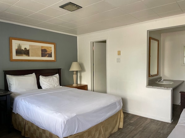 Quarto de hotel com uma cama grande, mesa de cabeceira com abajur, quadro emoldurado na parede e banheiro com espelho e pia.