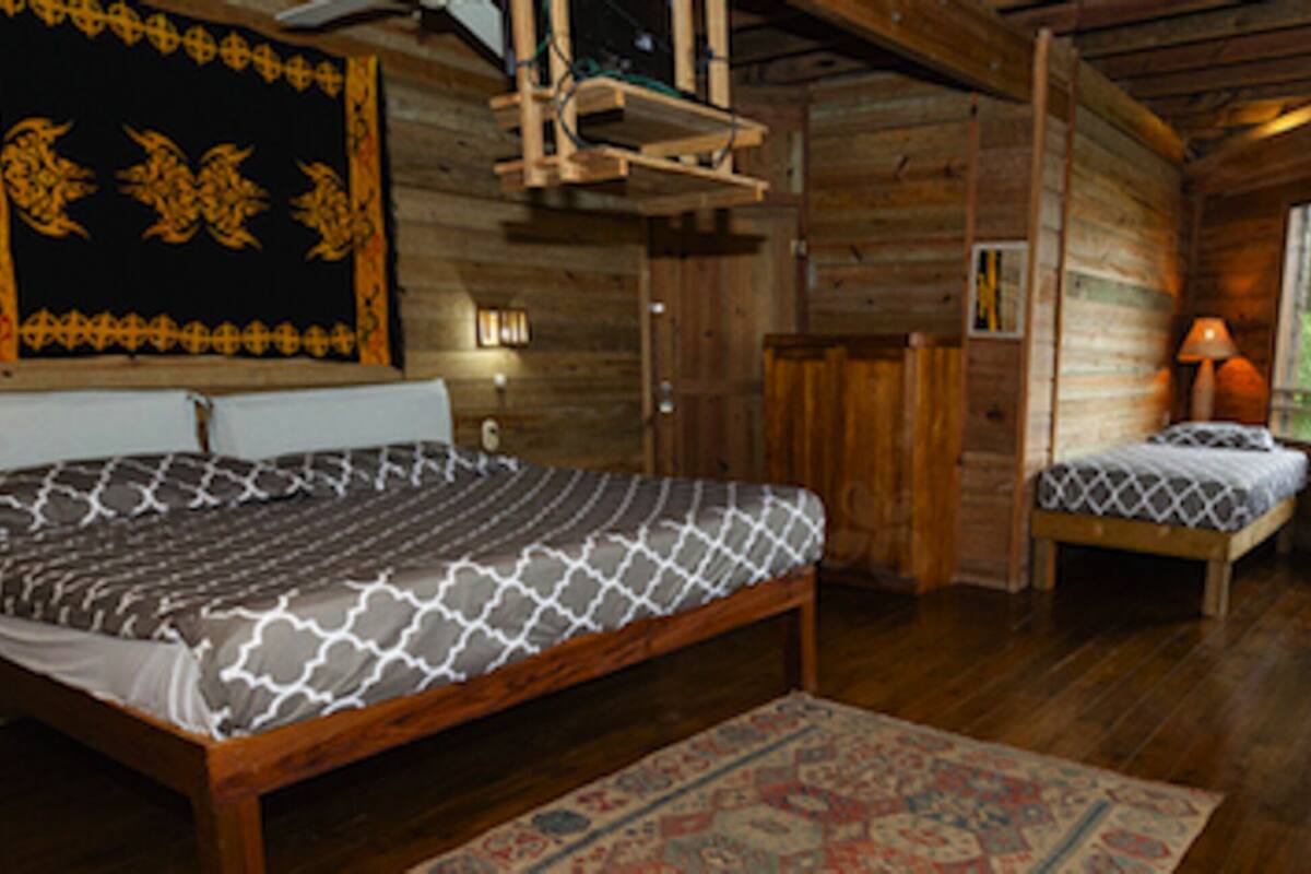 Quarto de cabana de toras com uma cama grande, uma cama menor, uma cadeira e uma escrivaninha.