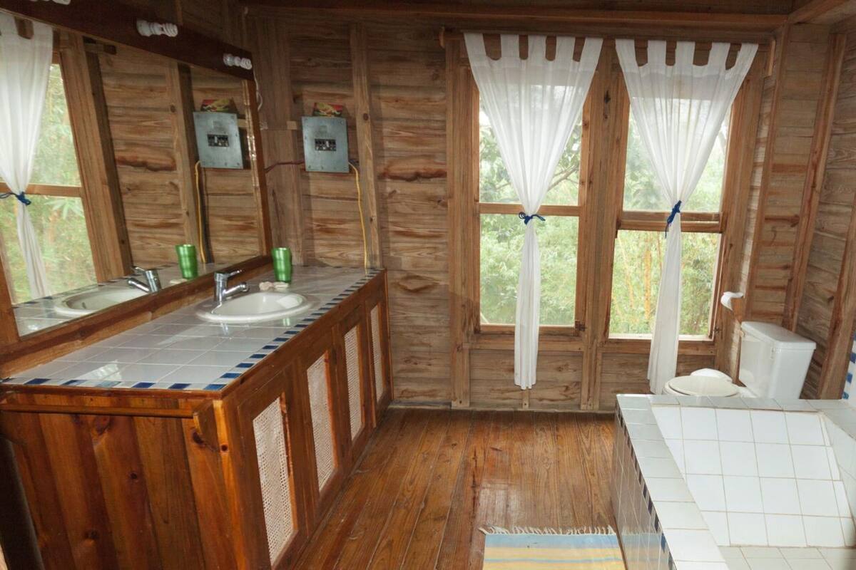 Casa de banho de cabana de madeira, com soalho de madeira, duas pias, sanita e banheira.