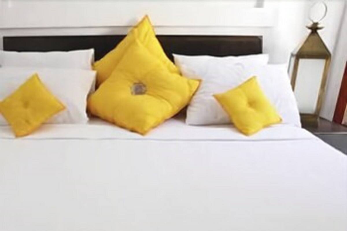 Cama com roupa de cama branca e três almofadas amarelas.