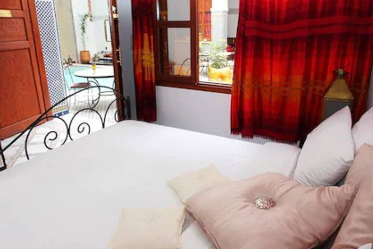 Quarto com cama, almofadas e janela com cortinas.