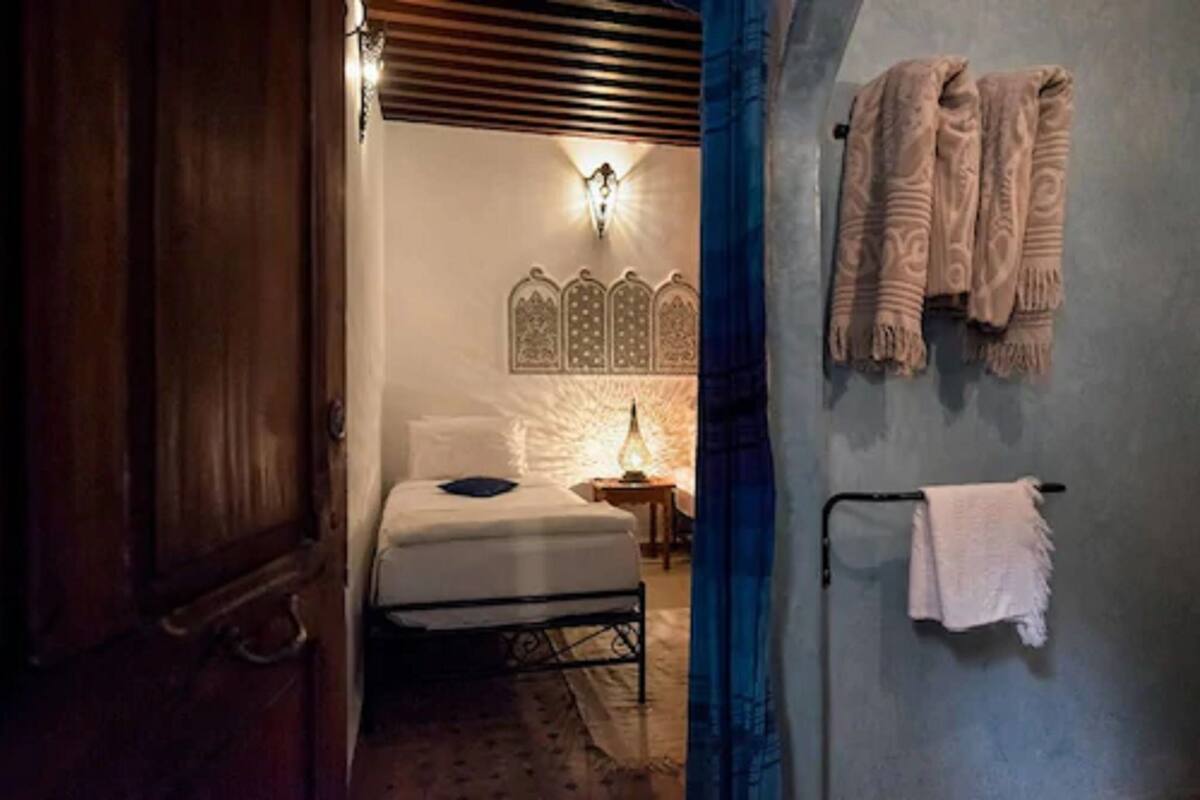 Quarto com cama, luminária na parede, mesa de cabeceira e porta-toalhas.