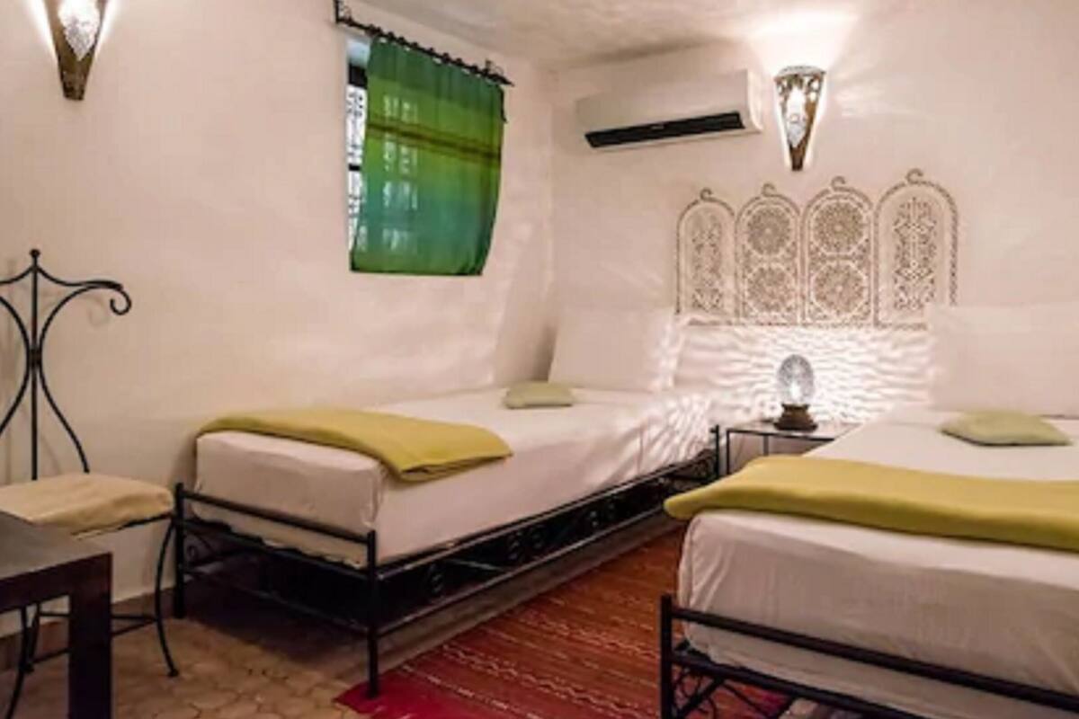 Quarto com duas camas, uma mesa pequena e uma janela com cortinas verdes.