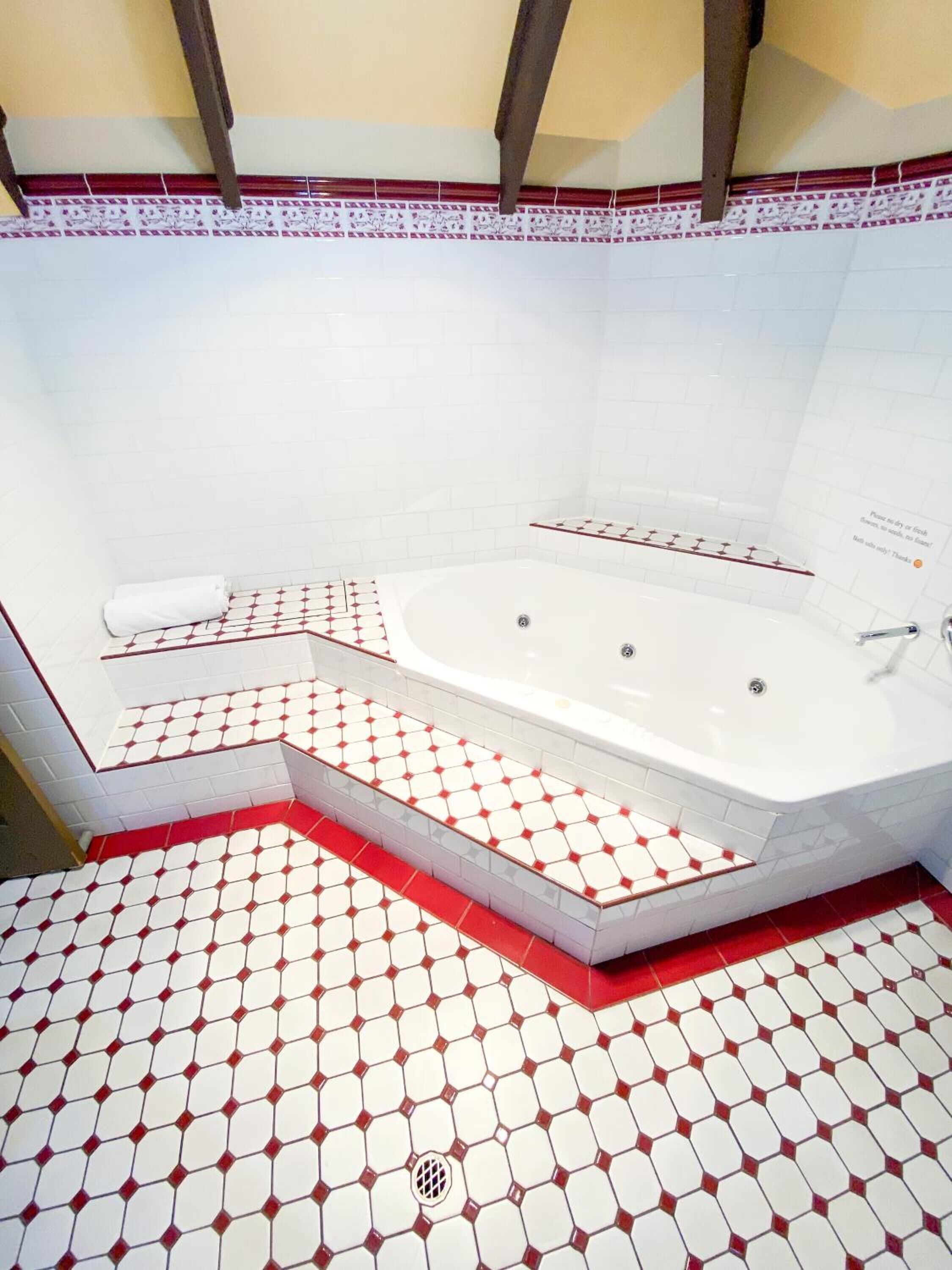 Um banheiro moderno com banheira de imersão, azulejos brancos e vermelhos estampados e um vigamento de madeira no teto.