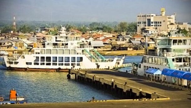 Um cais de ferryboat com um ferryboat grande, um cais e uma cidade ao fundo.