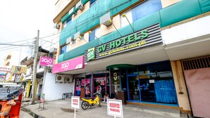 Um hotel com fachada verde e branca, entrada visível e placas indicando estacionamento reservado.