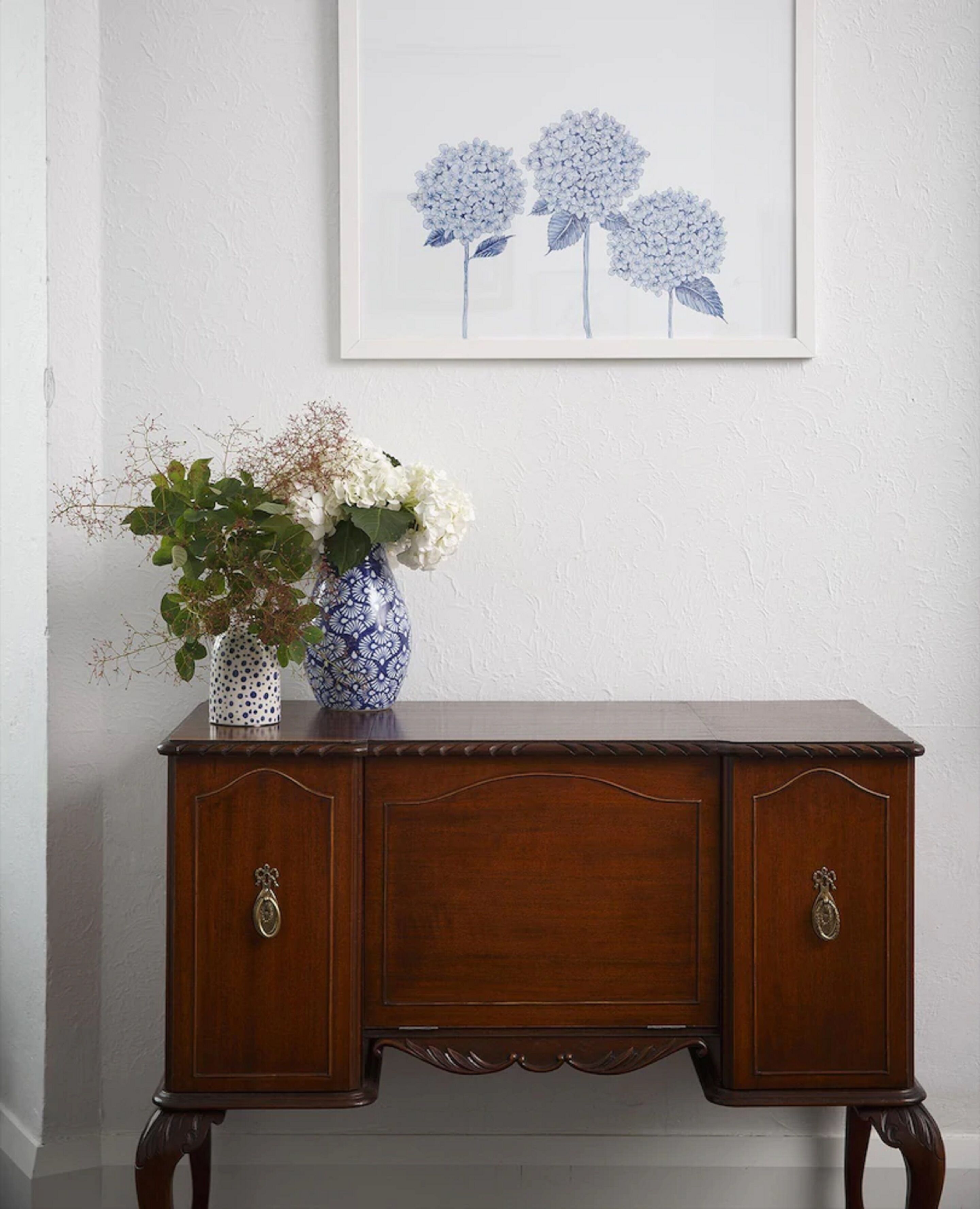 Um armário de madeira com um vaso de flores e um quadro na parede.
