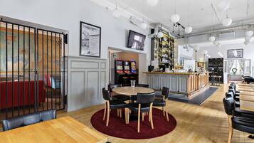Um restaurante moderno com área de bar, mesas de madeira e cadeiras de couro preto.