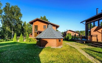 Uma cabana de madeira com telhado inclinado, cercada por um gramado bem cuidado e árvores.