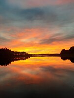 Um lago tranquilo refletindo um pôr do sol com uma orla arborizada.