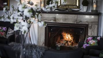 Uma lareira com fogo, um espelho acima e um vaso com flores em primeiro plano.