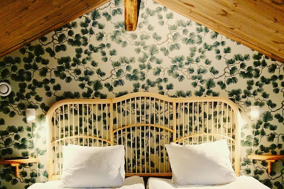 Cama com cabeceira de madeira e almofadas brancas num quarto com papel de parede estampado.