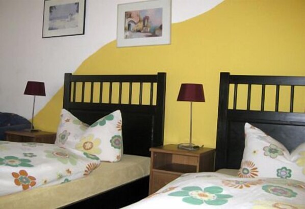 Quarto com duas camas, cada uma com roupa de cama florida e cabeceiras de madeira. Há duas mesas de cabeceira com luminárias.